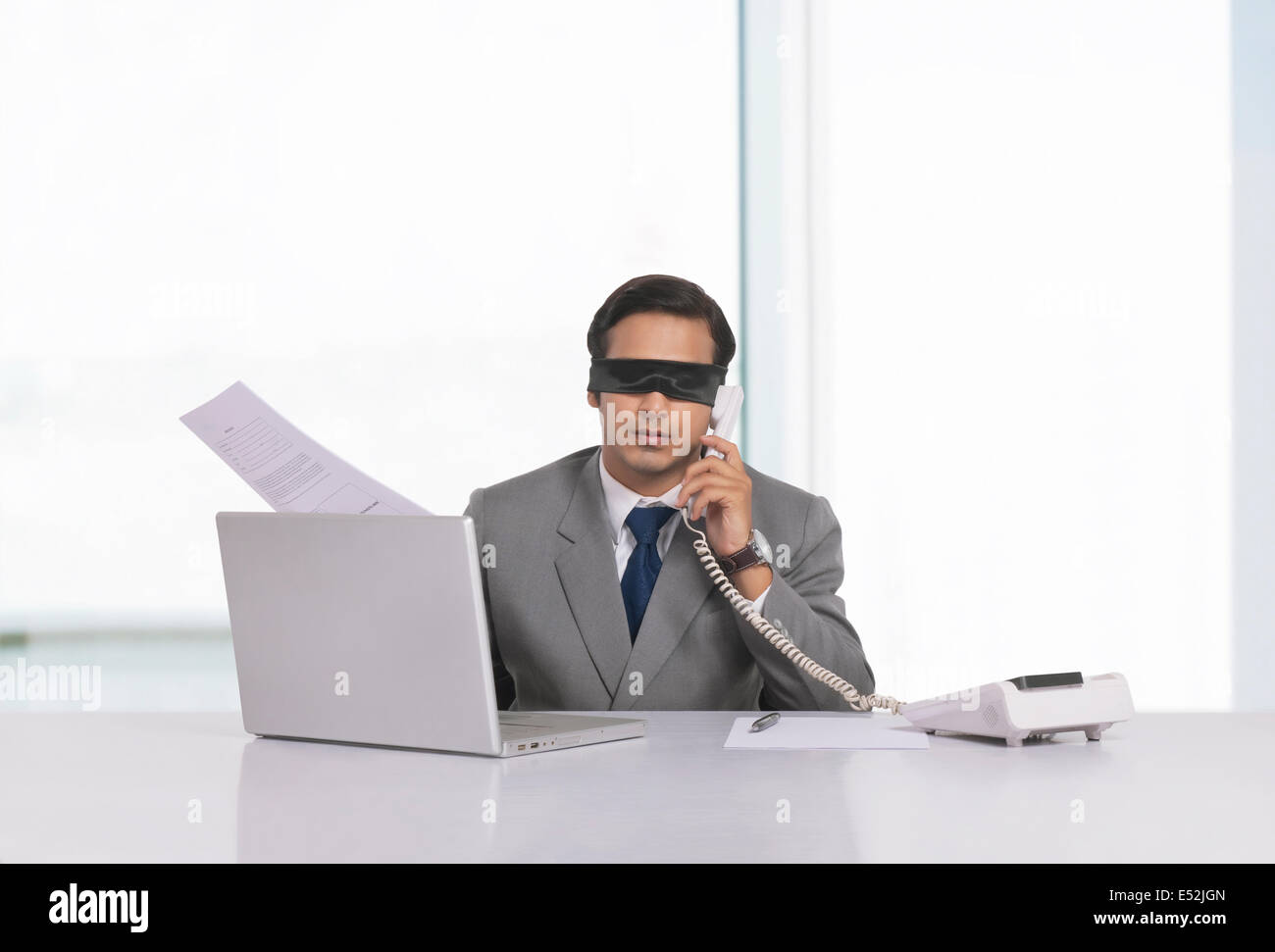 Blindfolded businessman working at desk in office Stock Photo - Alamy
