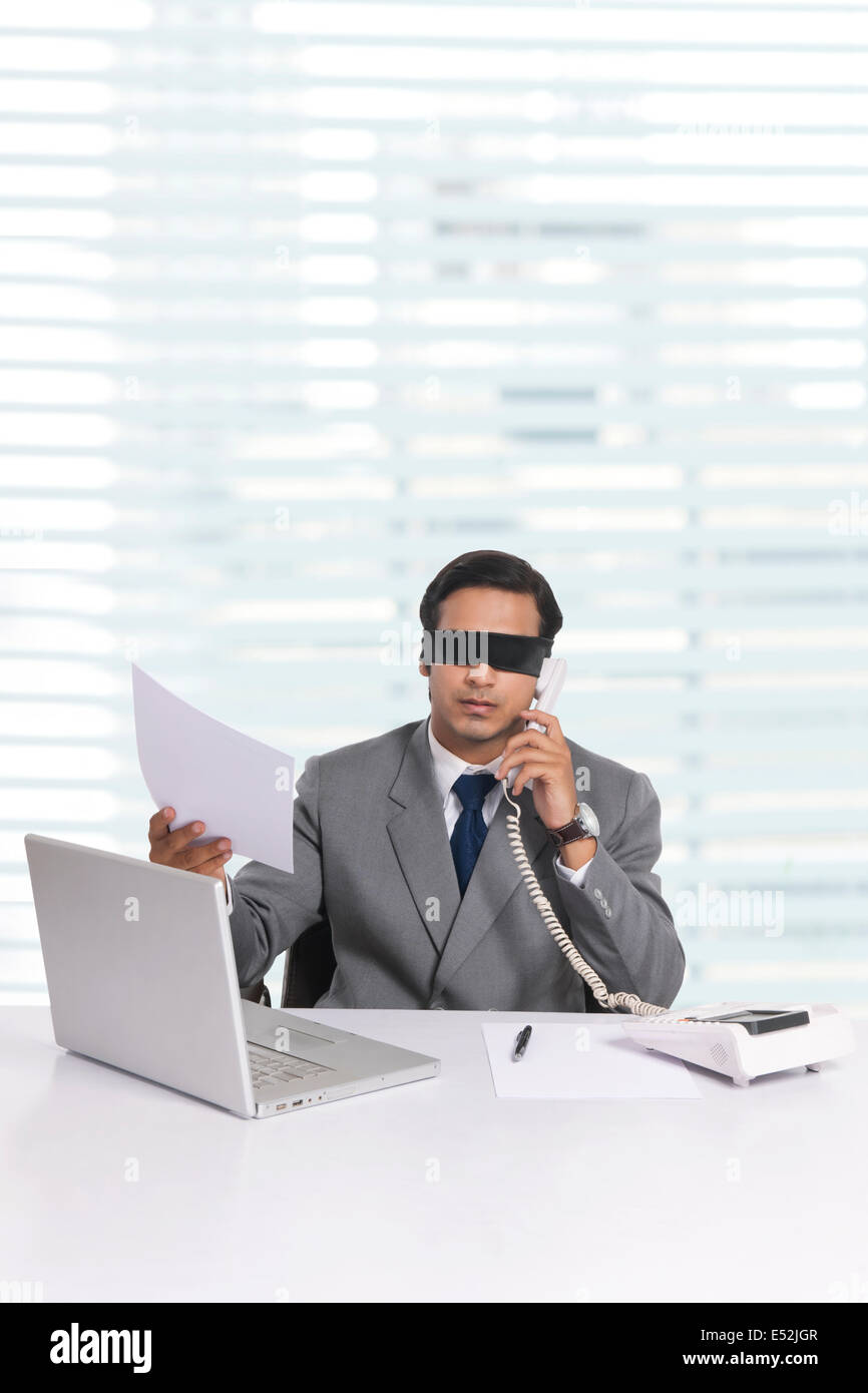 Blindfolded young businessman working at office desk Stock Photo - Alamy