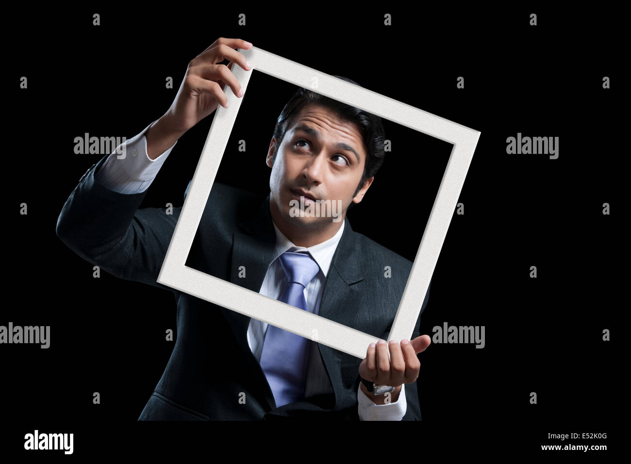 Confused businessman holding picture frame against black background ...
