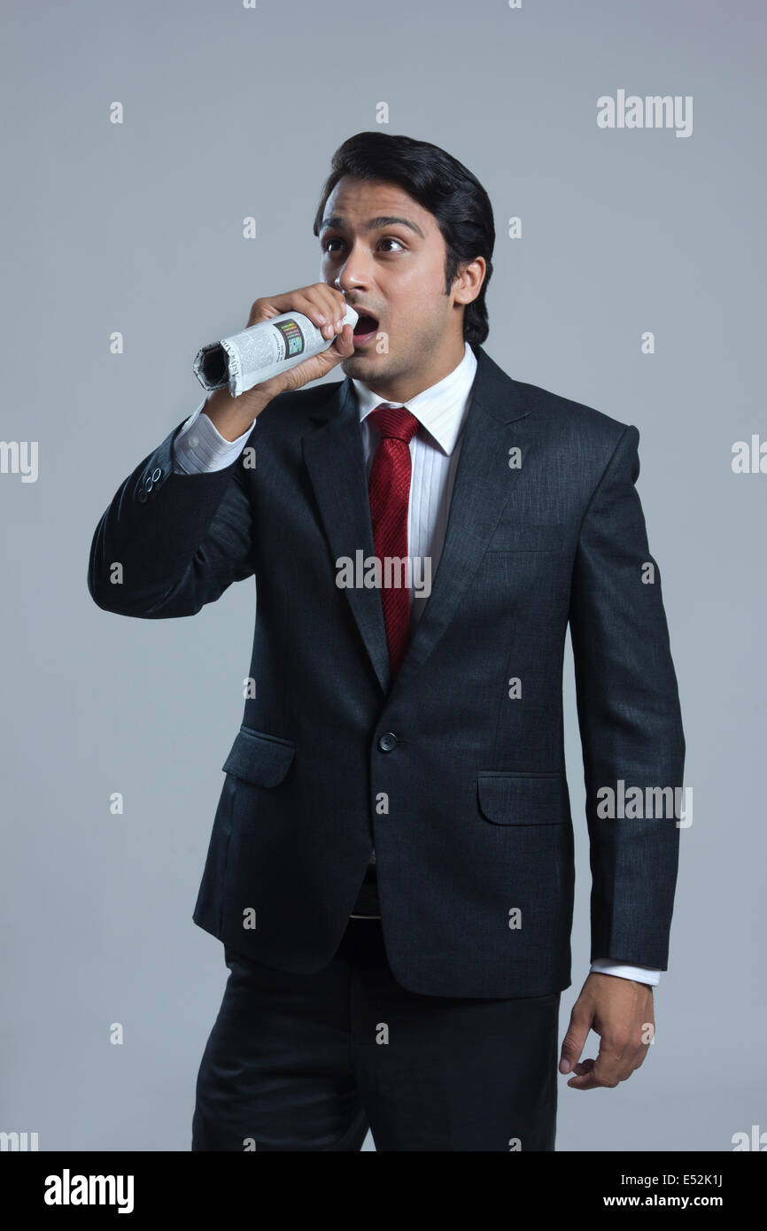 Angry businessman screaming through newspaper over gray background ...