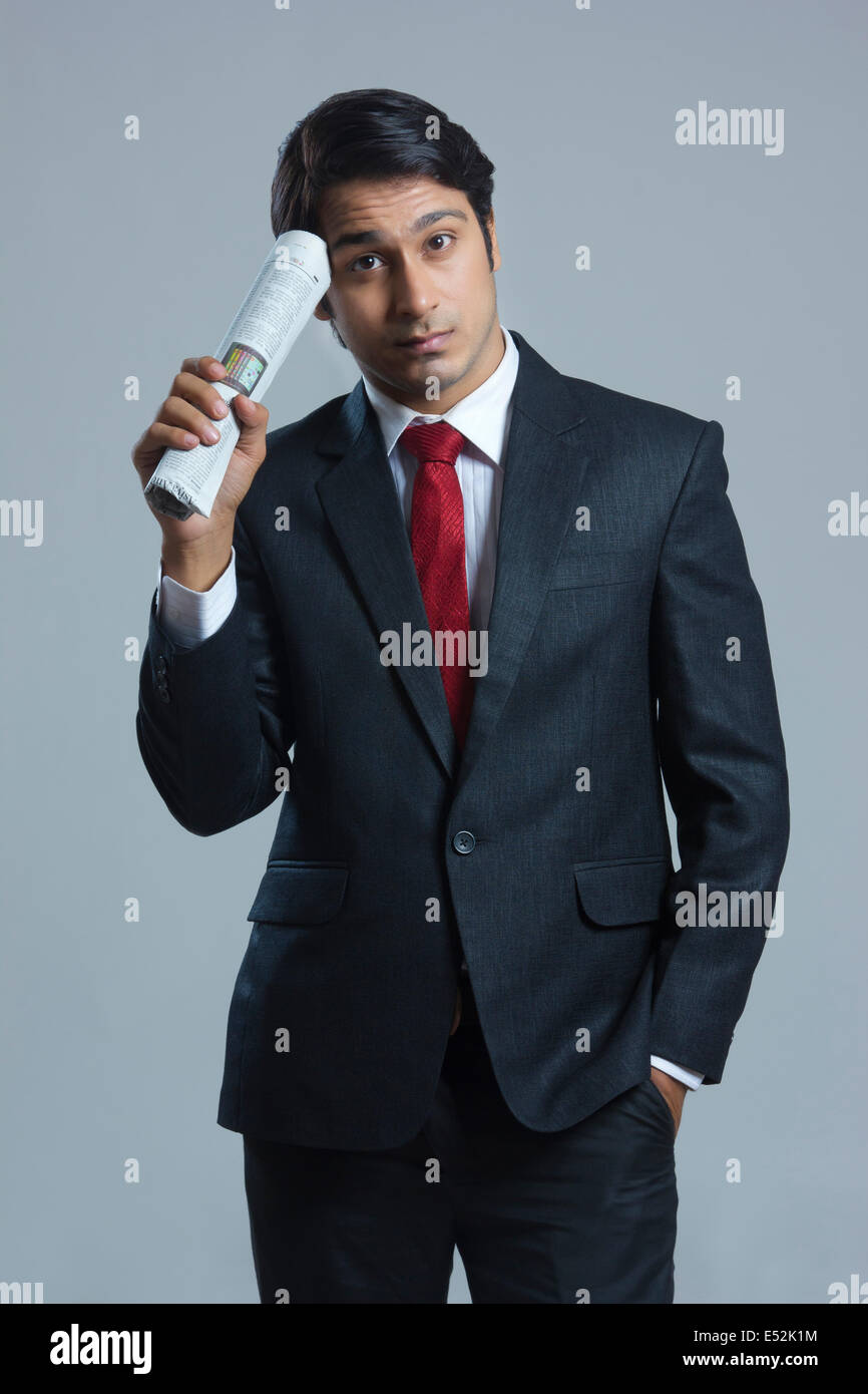 Portrait of confused businessman holding newspaper over gray background ...