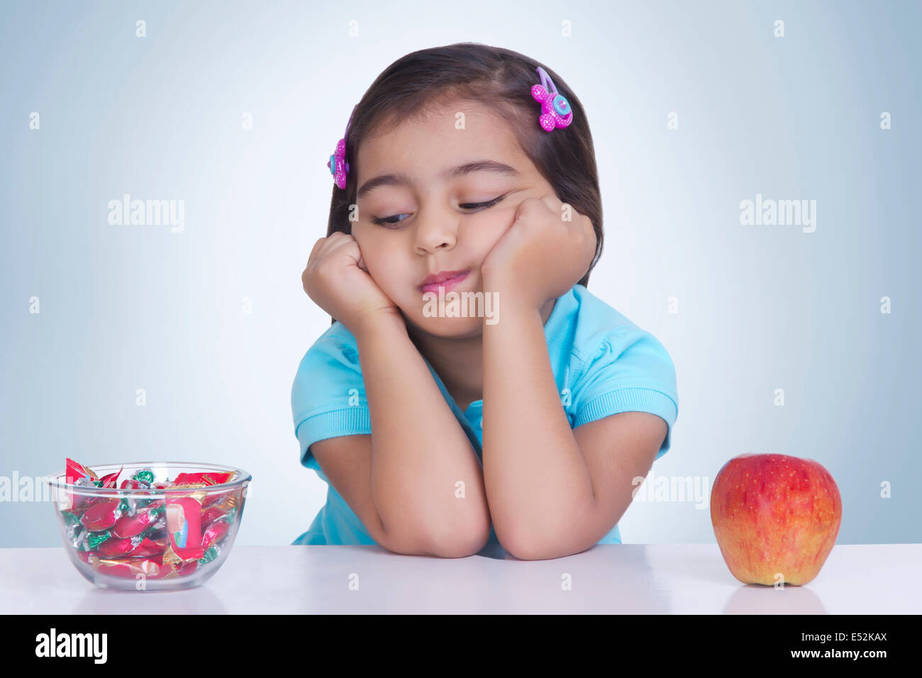 Girl choosing between sweet food and apple against blue background ...