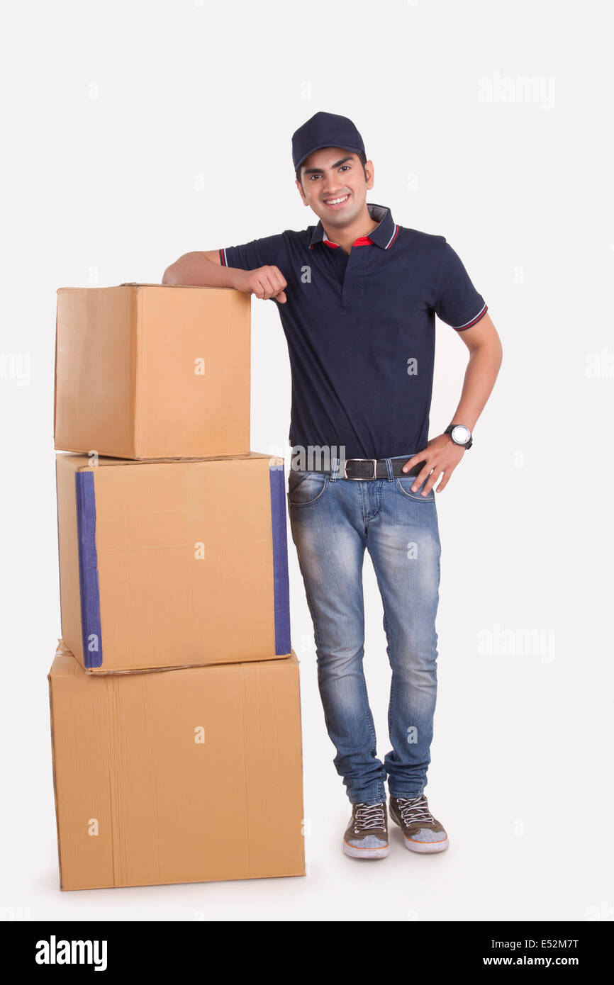 Full length portrait of confident delivery man with stacked packages ...