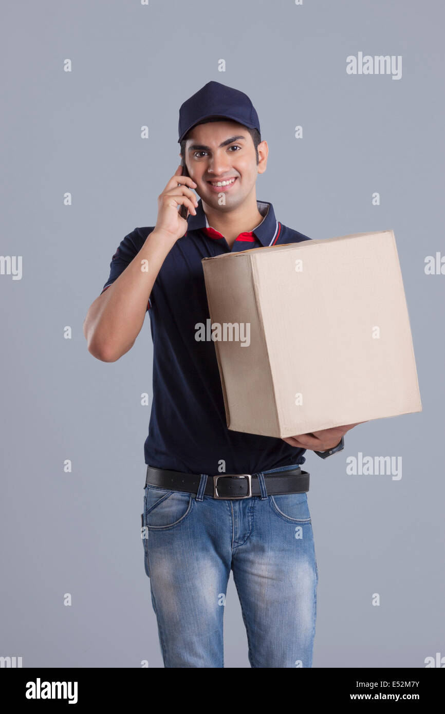 Portrait of delivery man carrying package while answering mobile phone ...