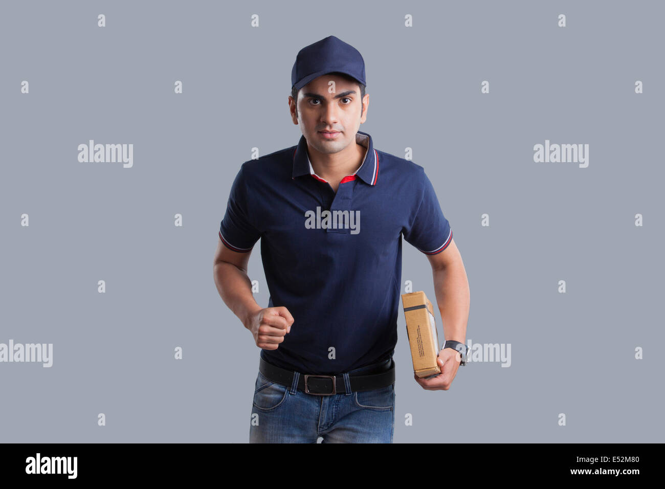 Portrait of delivery man running with package against gray background ...