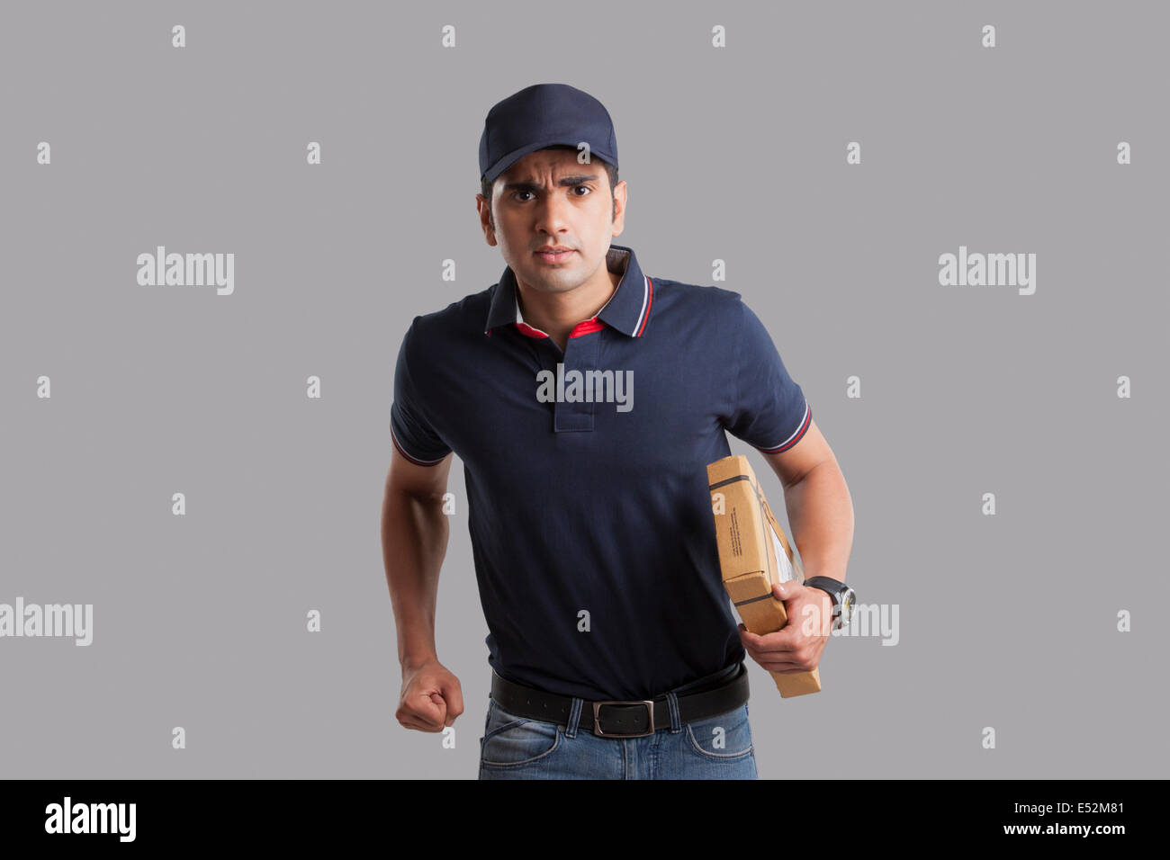 Portrait of confident delivery man running with package over gray ...