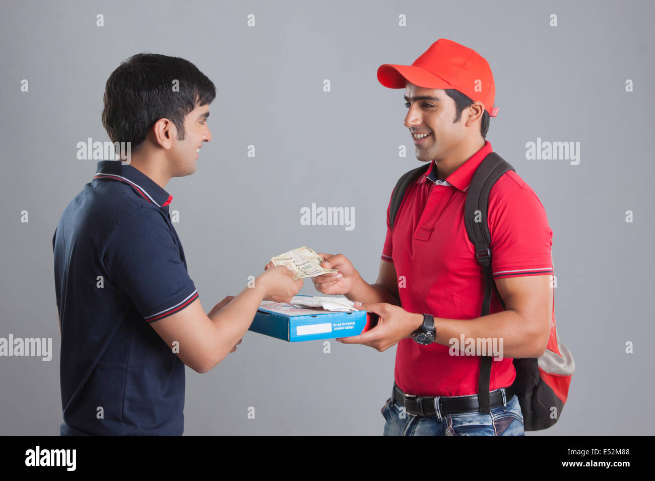 Smiling delivery man delivering pizza to customer against gray ...