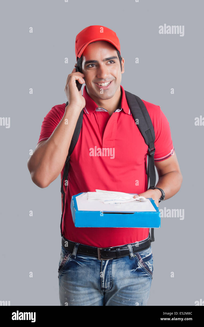 Happy pizza delivery man answering mobile phone against gray background ...