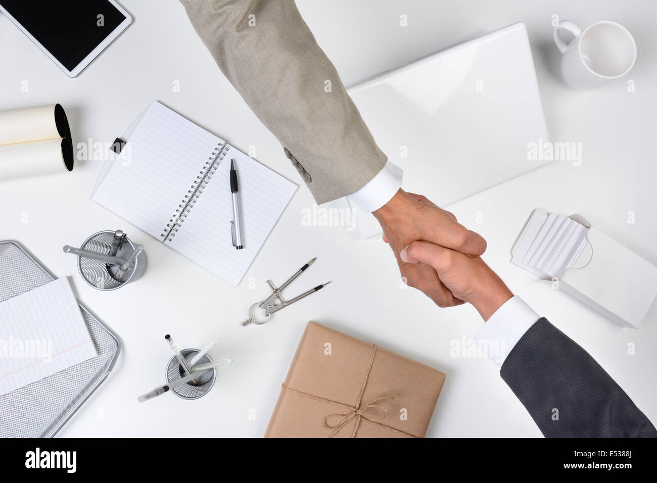 Two men reaching over a desk to shake hands. Shot from a high angle the ...