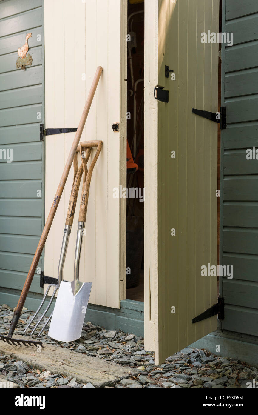 Garden fork, spade and rake, leaning against a wooden, painted shed ...
