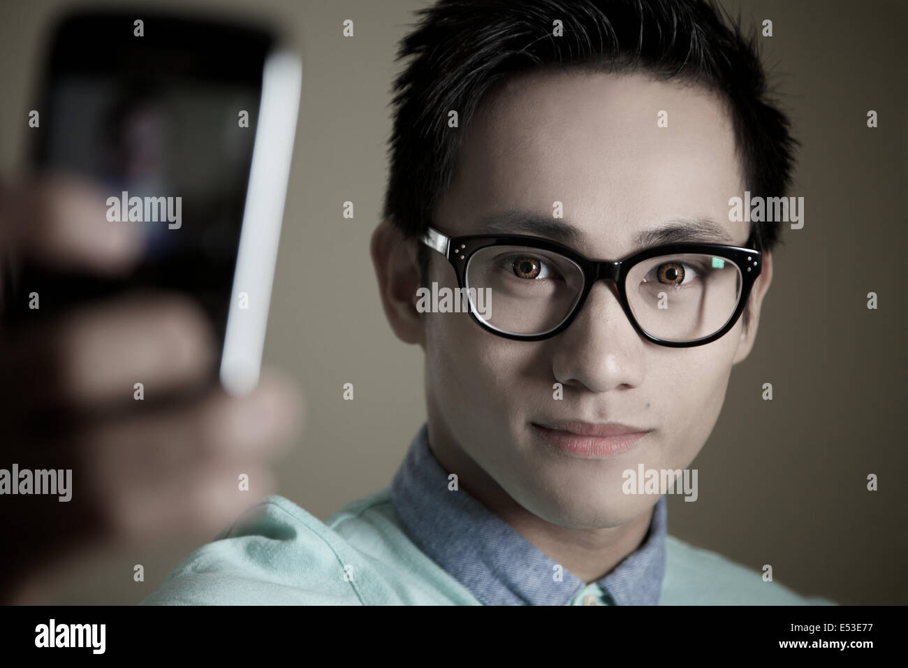 A young guy taking a selfie on his phone in a mirror. Wearing coloured ...