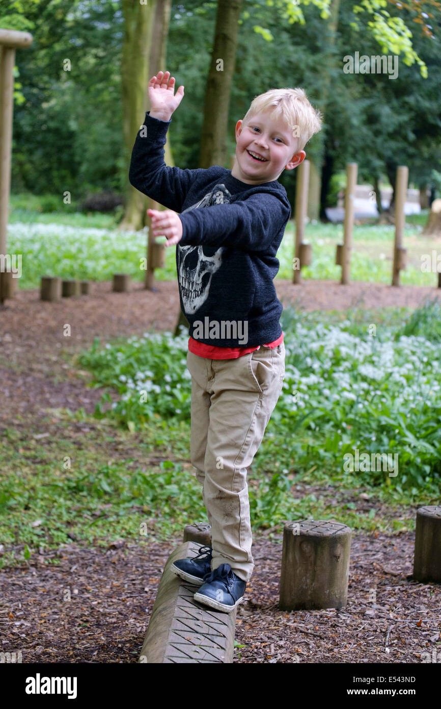 Blond Boy aged six laughing as he is balancing on adventure playground ...