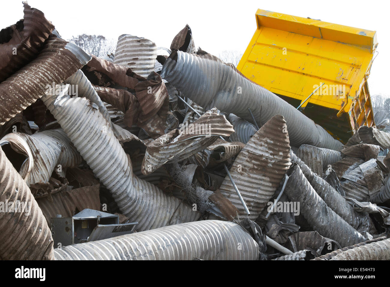 Scrap heap of rusting discarded drainage pipes with yellow tractor ...