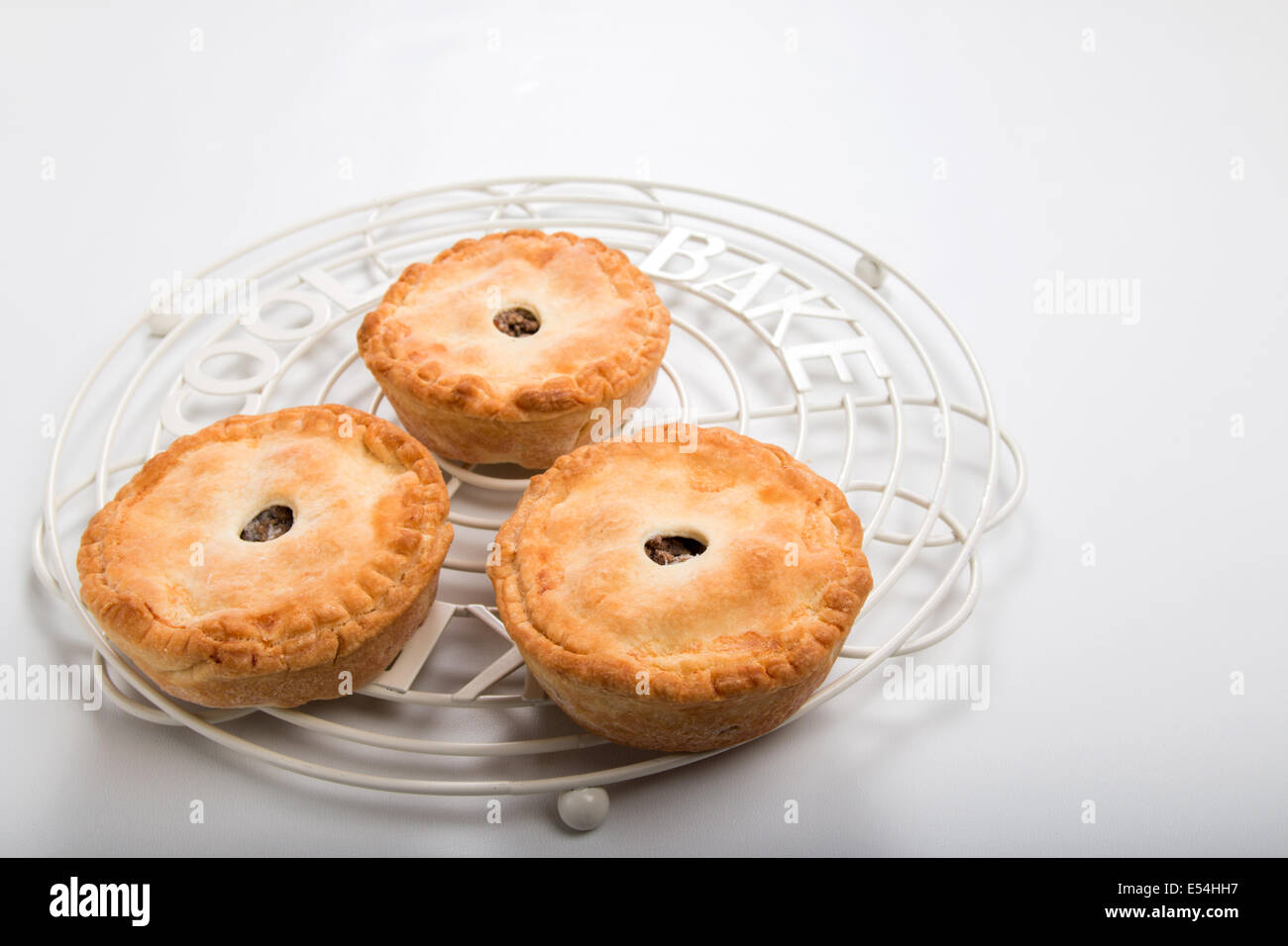 3 small homemade meat pies on a round cooling rack on a pale background ...