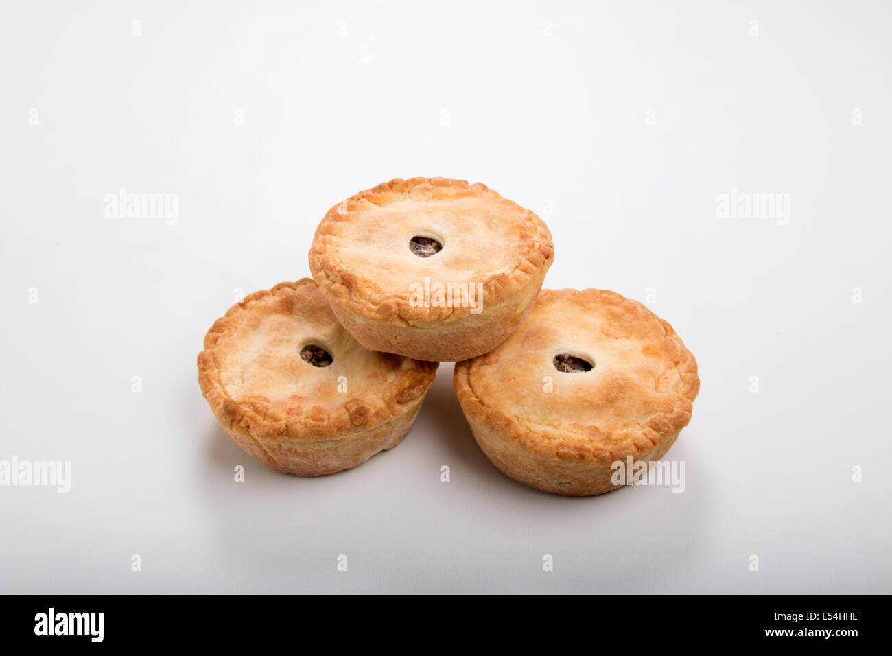 3 small homemade meat pies in a stack on a pale background individual ...