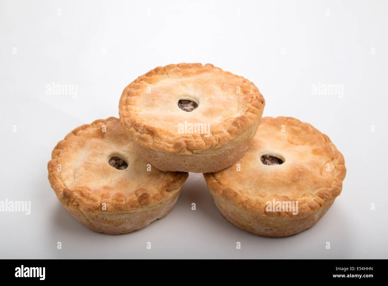 3 small homemade meat pies in a stack on a pale background individual ...