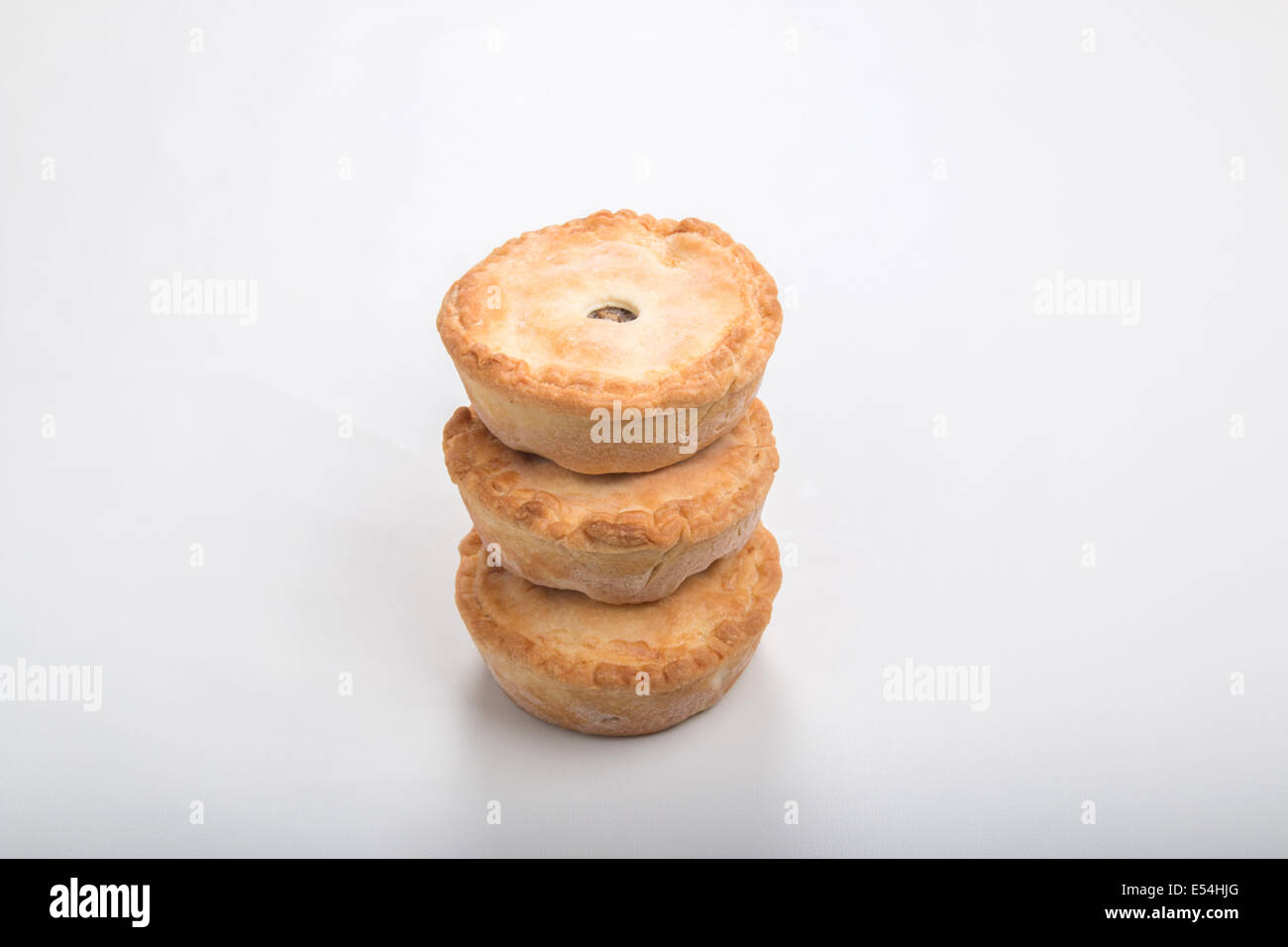 3 small meat pies in a vertical stack on a pale background individual ...