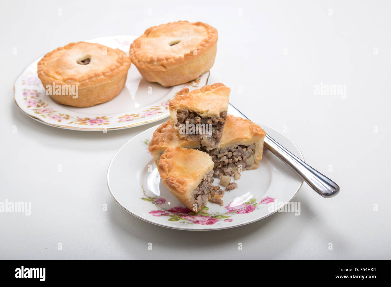 Small meat pies on flowered plates, knife on the plate , cut to show ...