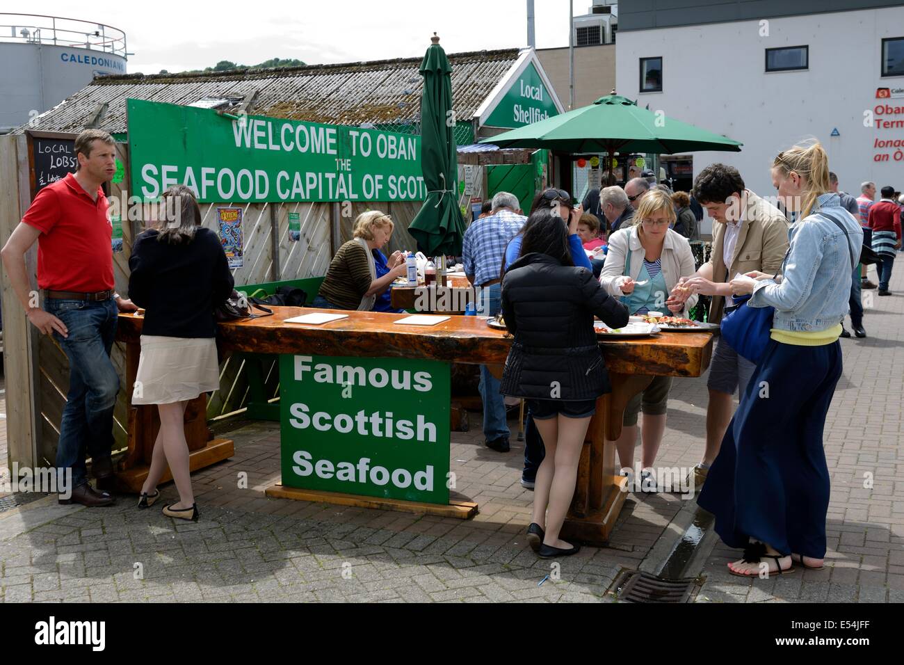 People eating local fresh seafood from a shop on the pier in Oban ...