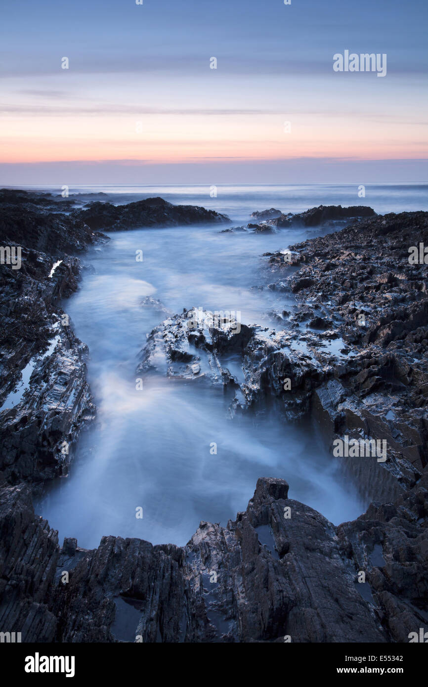 View of sea washing into large rockpool during incoming tide at sunset ...