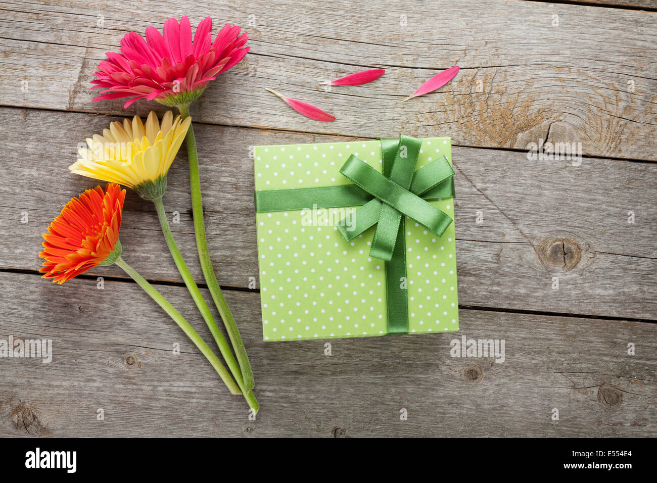 Three colorful gerbera flowers with gift box on wooden table Stock ...