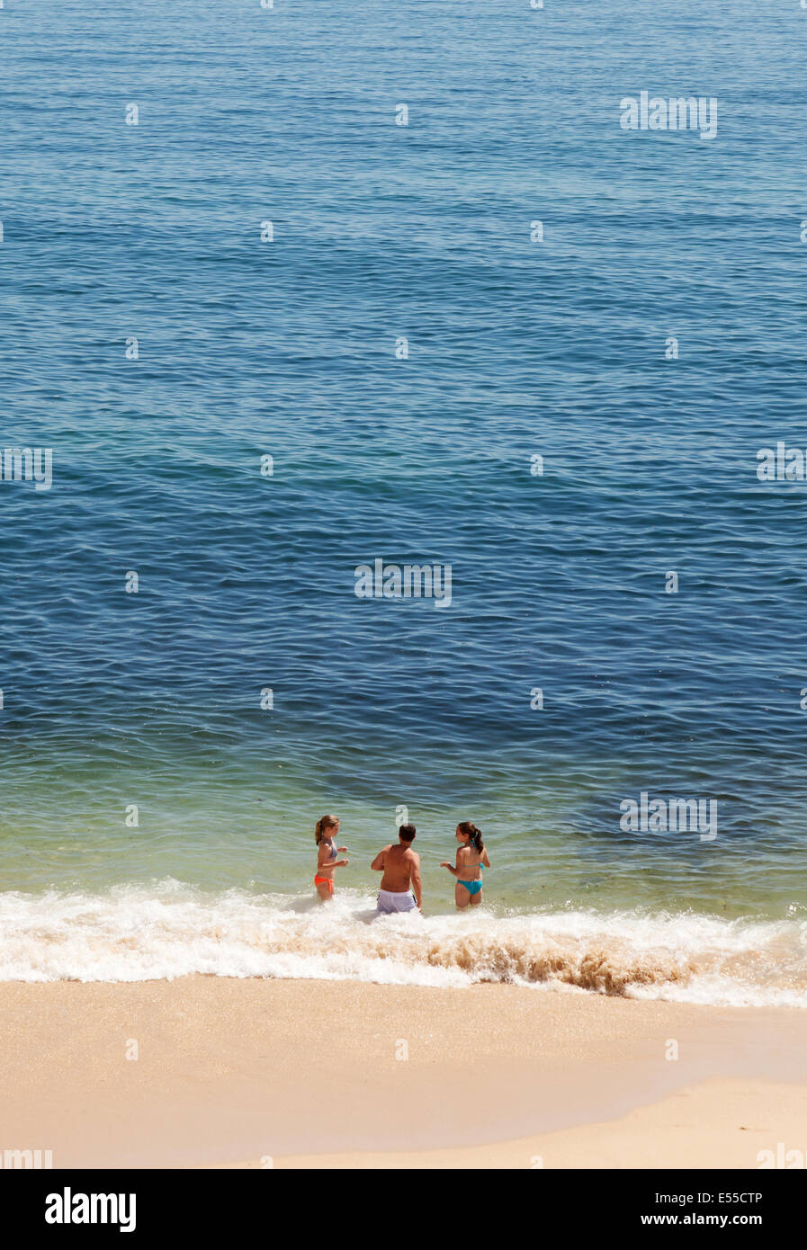 Three people on a beach at the waters edge on a summer holiday, Vale ...