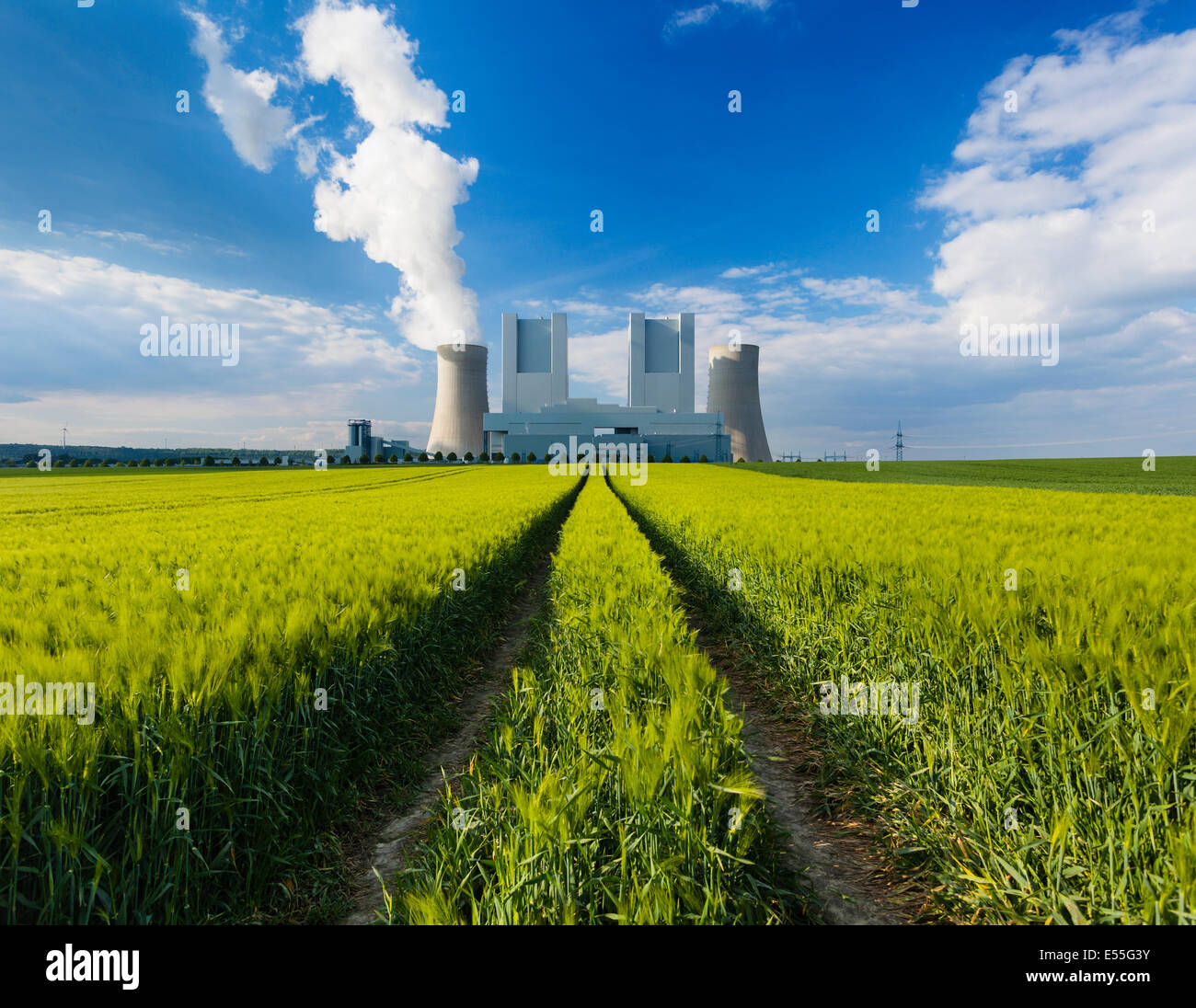 A shiny new lignite power station behind a rye field with wheel tracks ...