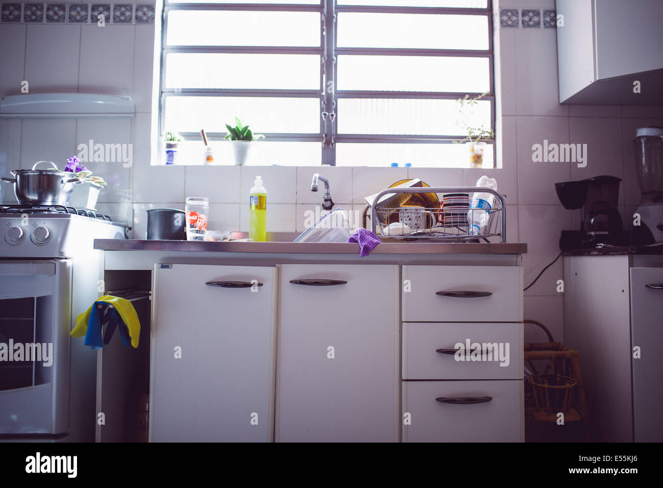 Domestic kitchen with sink, counter and scattered crockery and a window ...