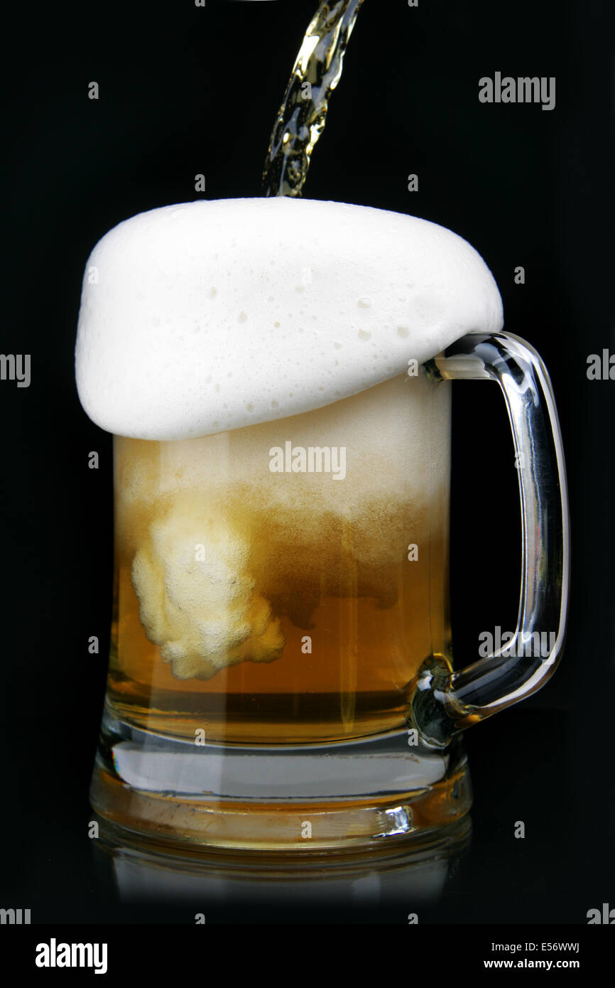 Pouring beer into mug over black background Stock Photo - Alamy