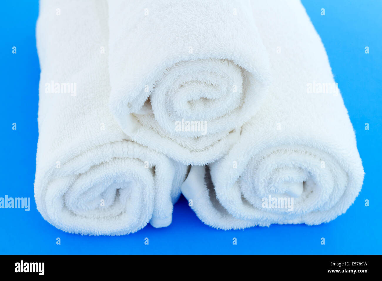 Three large white cotton bath cloths rolled up individually and piled ...