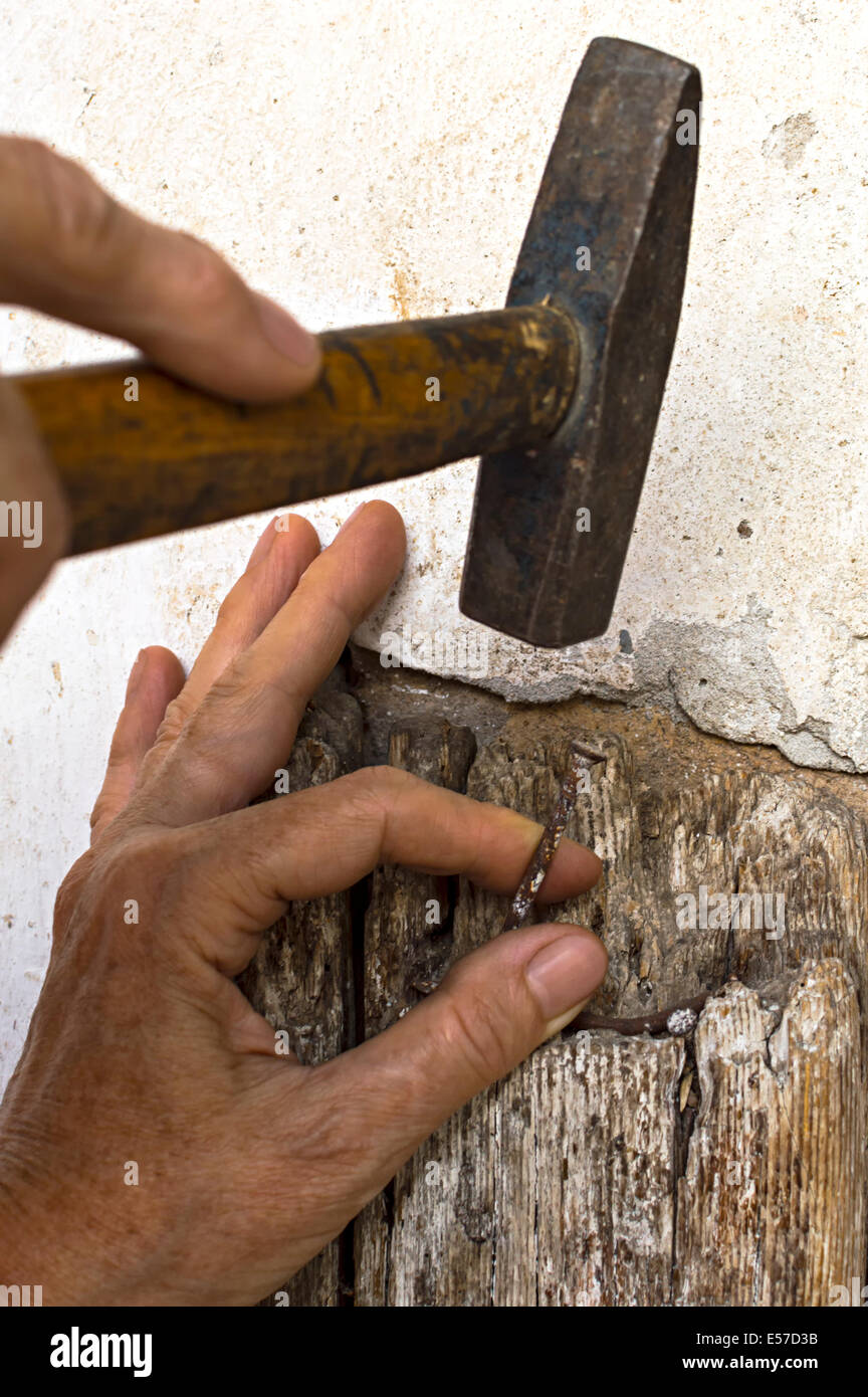 Hand holds a nail while hitting it with a hammer Stock Photo - Alamy