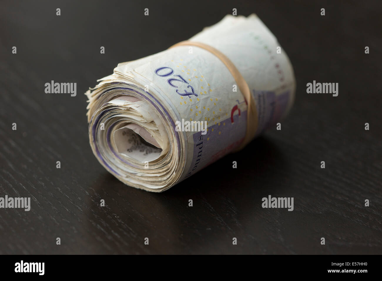 roll of UK money on a black background with a rubber band around Stock ...