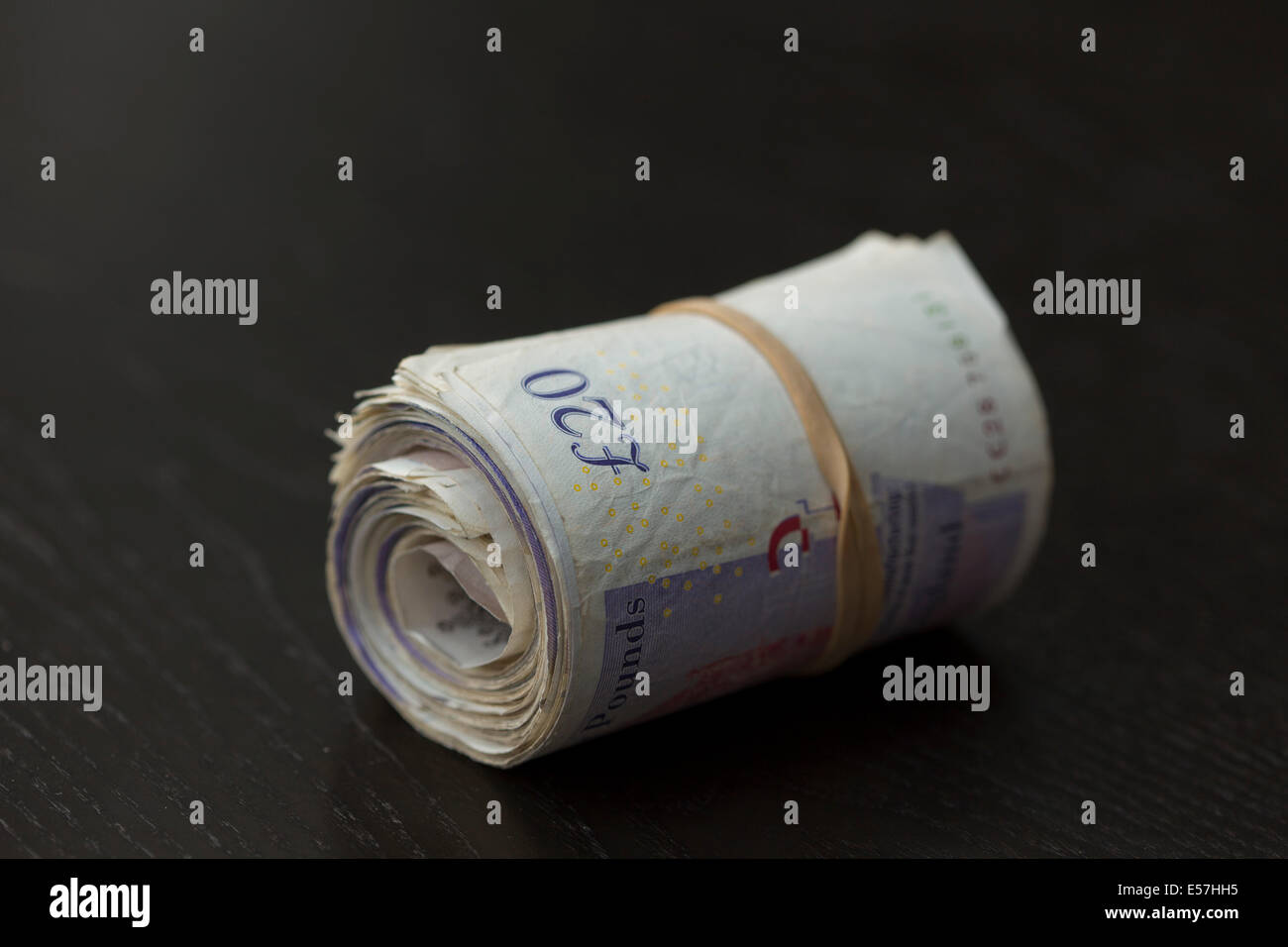 roll of UK money on a black background with a rubber band around Stock ...