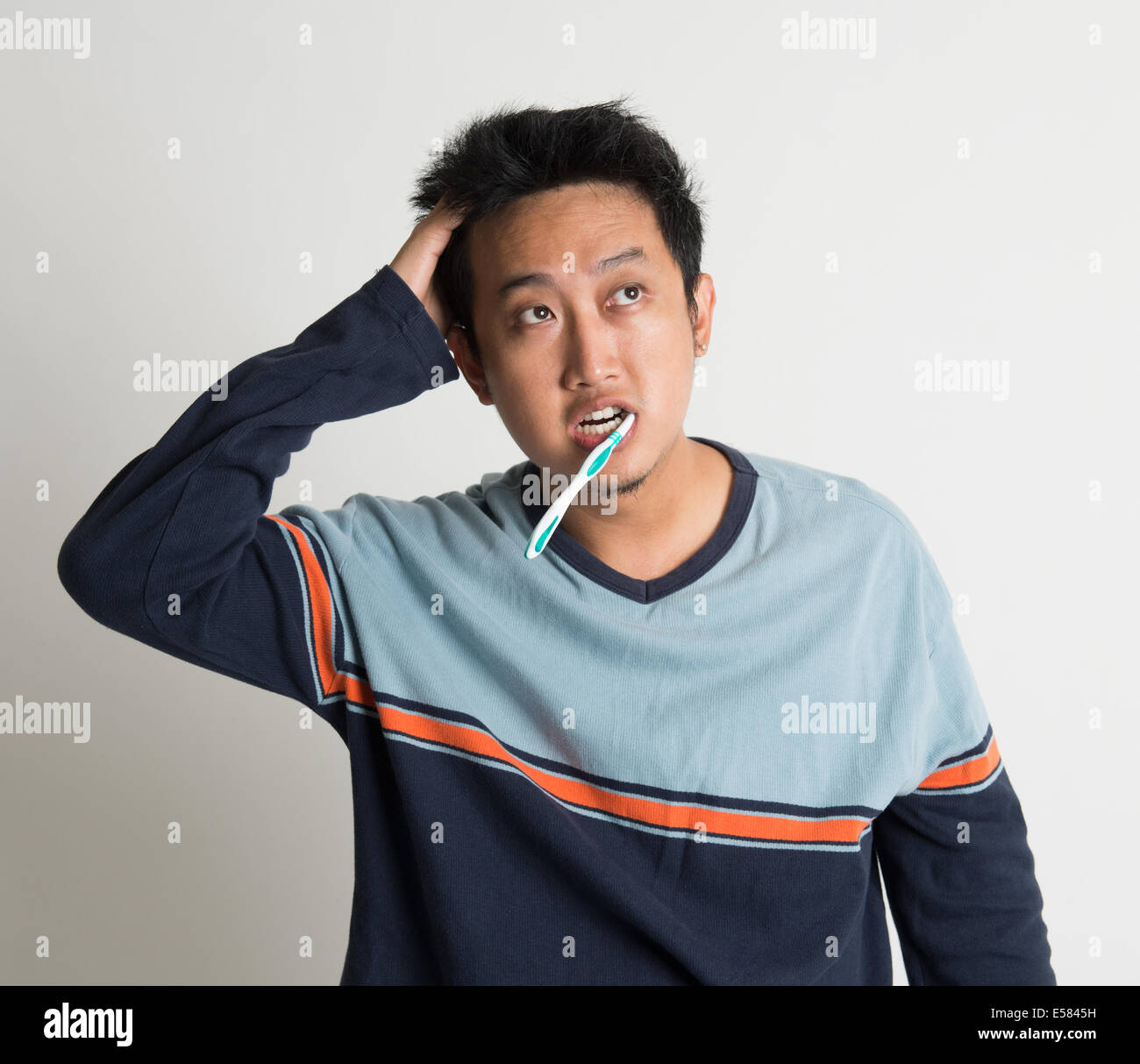 Southeast Asian male scratching head and looking up while brushing ...