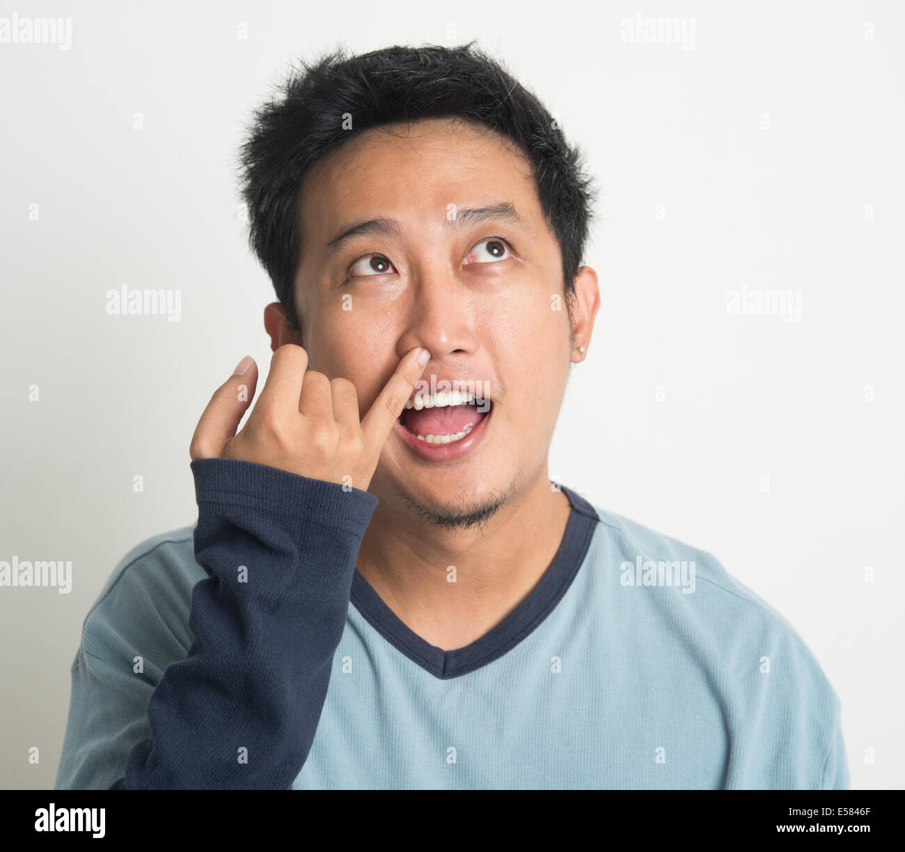 Disgusting Asian man picking nose with eyes looking up, on plain ...