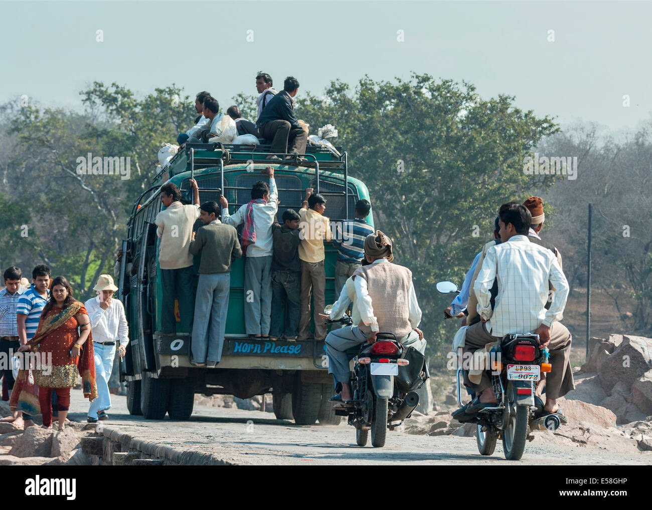 Overloaded public transport bus carrying people on top and hanging out ...