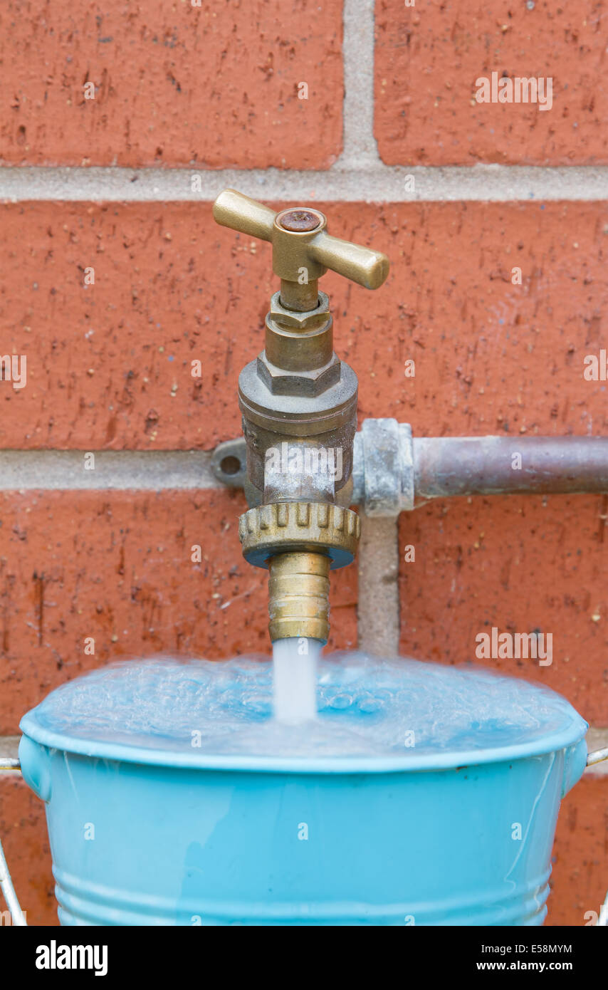 Outside tap on brick wall filling a blue bucket Stock Photo - Alamy