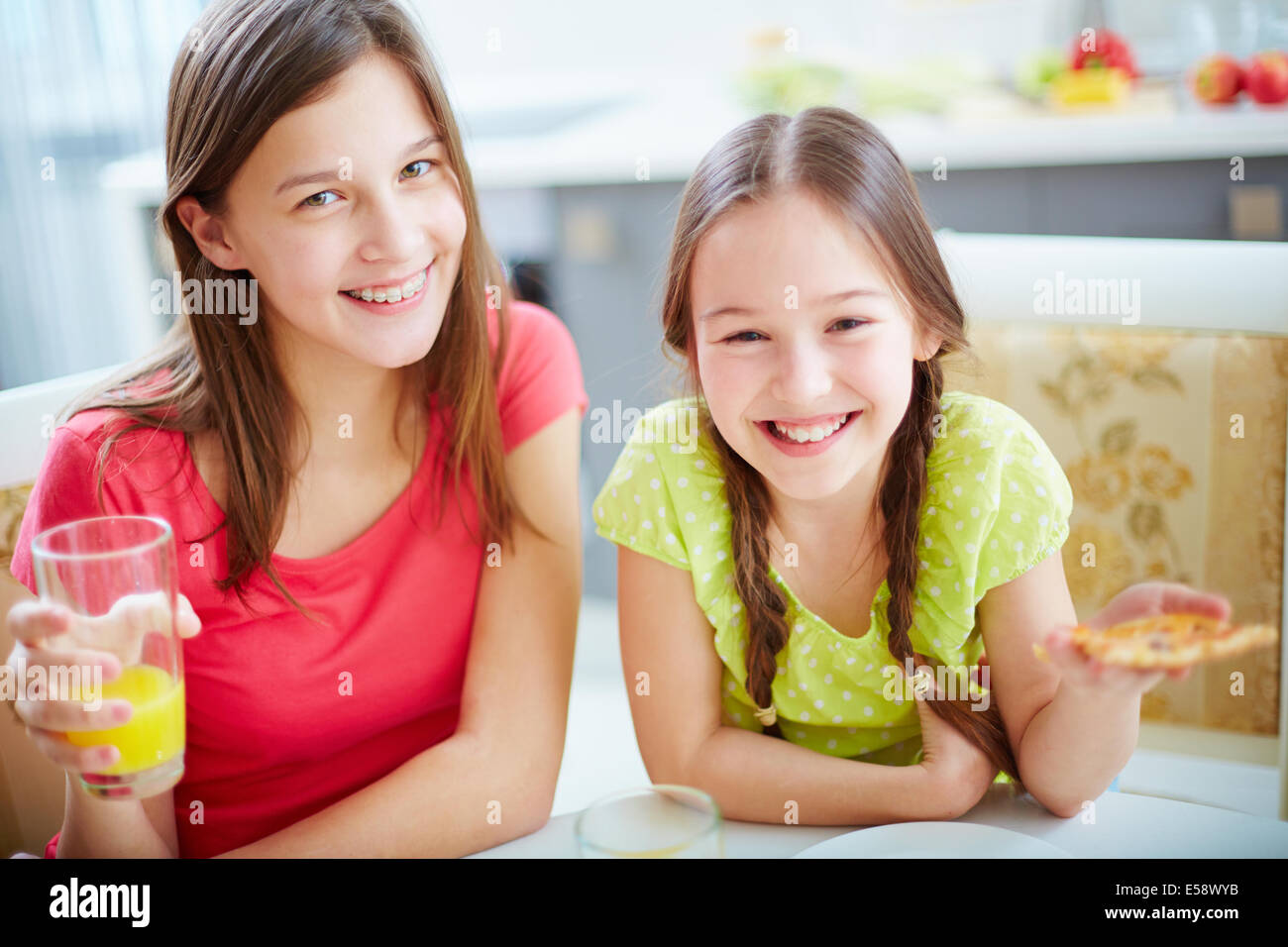Portrait of cute girls sitting by dinner table and looking at camera ...