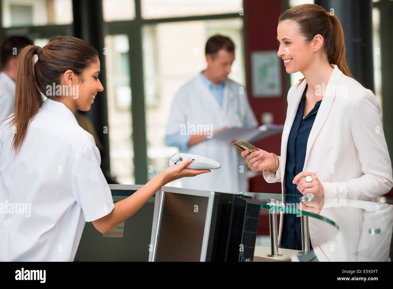 Female doctor making payment with credit card at hospital reception ...