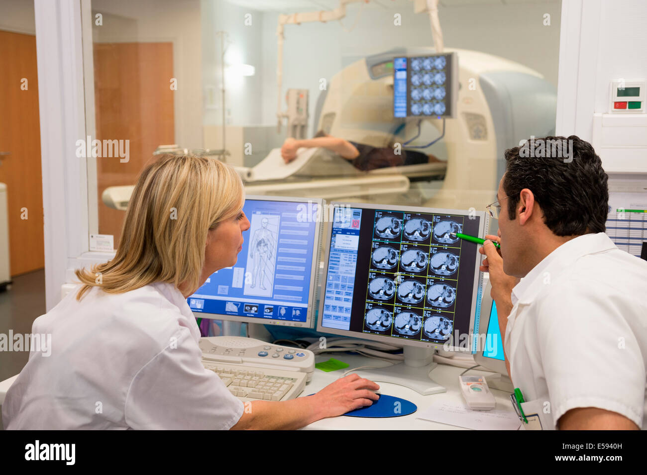 Doctors examining scan on computer with patient on MRI scanner in ...