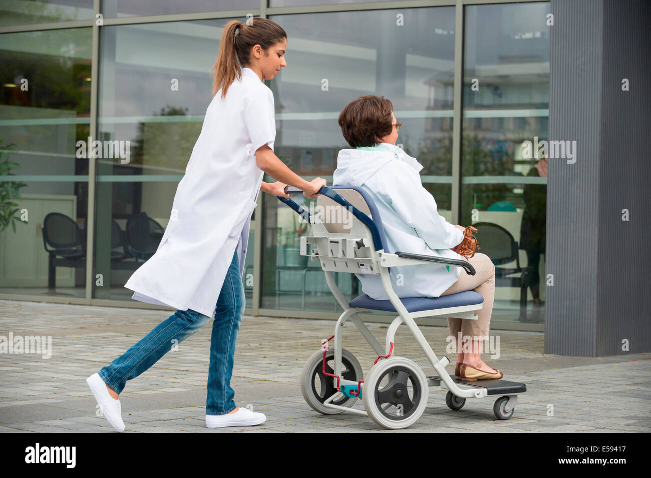 Female doctor pushing a patient sitting in a chair Stock Photo - Alamy
