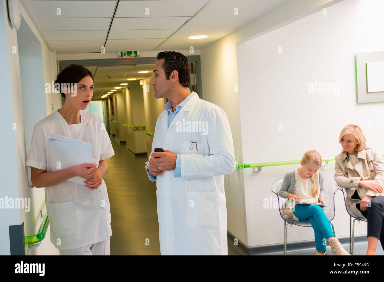 Doctor and nurse discussing in hospital corridor with patients sitting ... Doctor and nurse discussing in hospital corridor with patients sitting ...