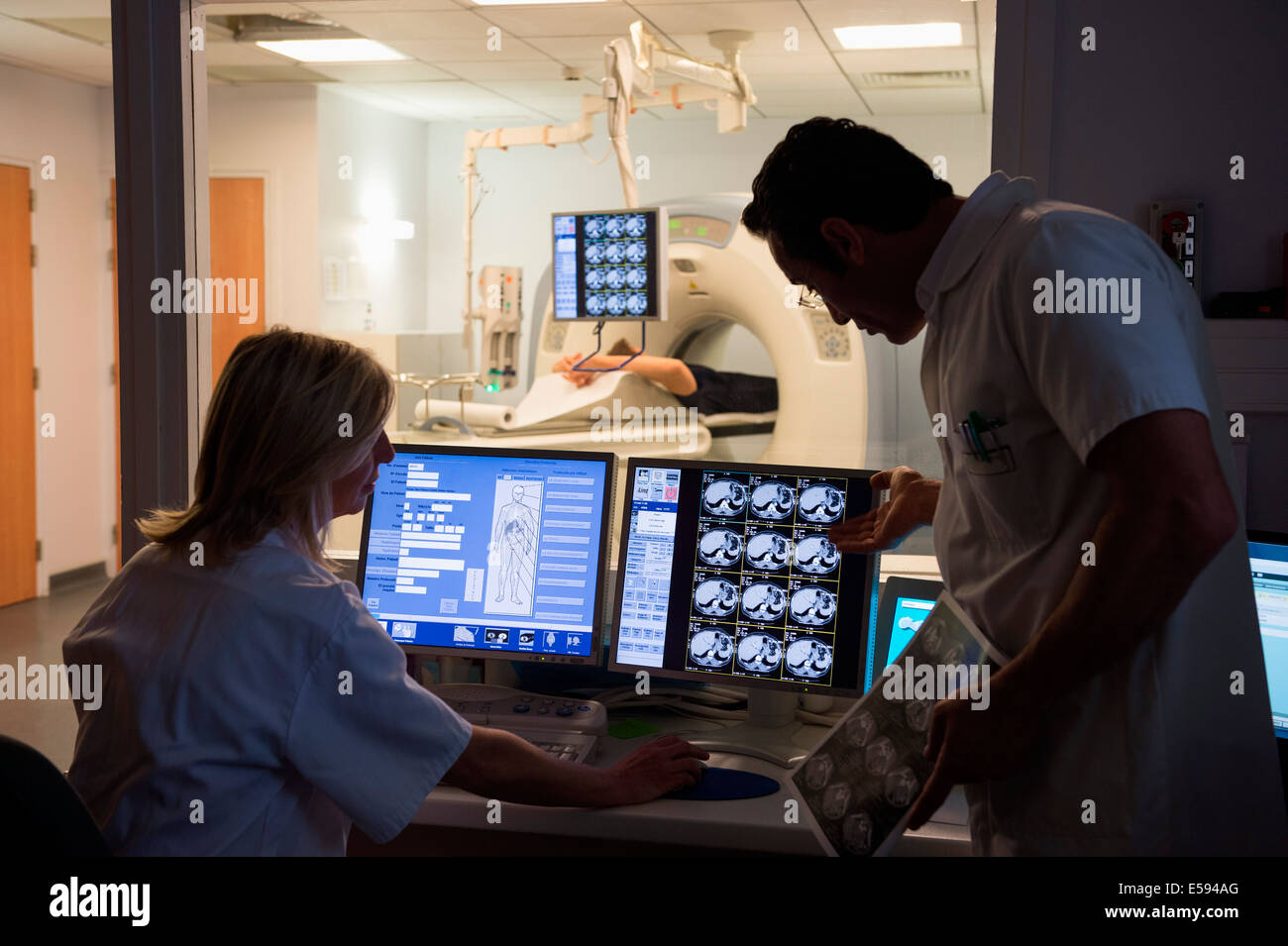 Doctors examining scan on computer with patient on MRI scanner in ...