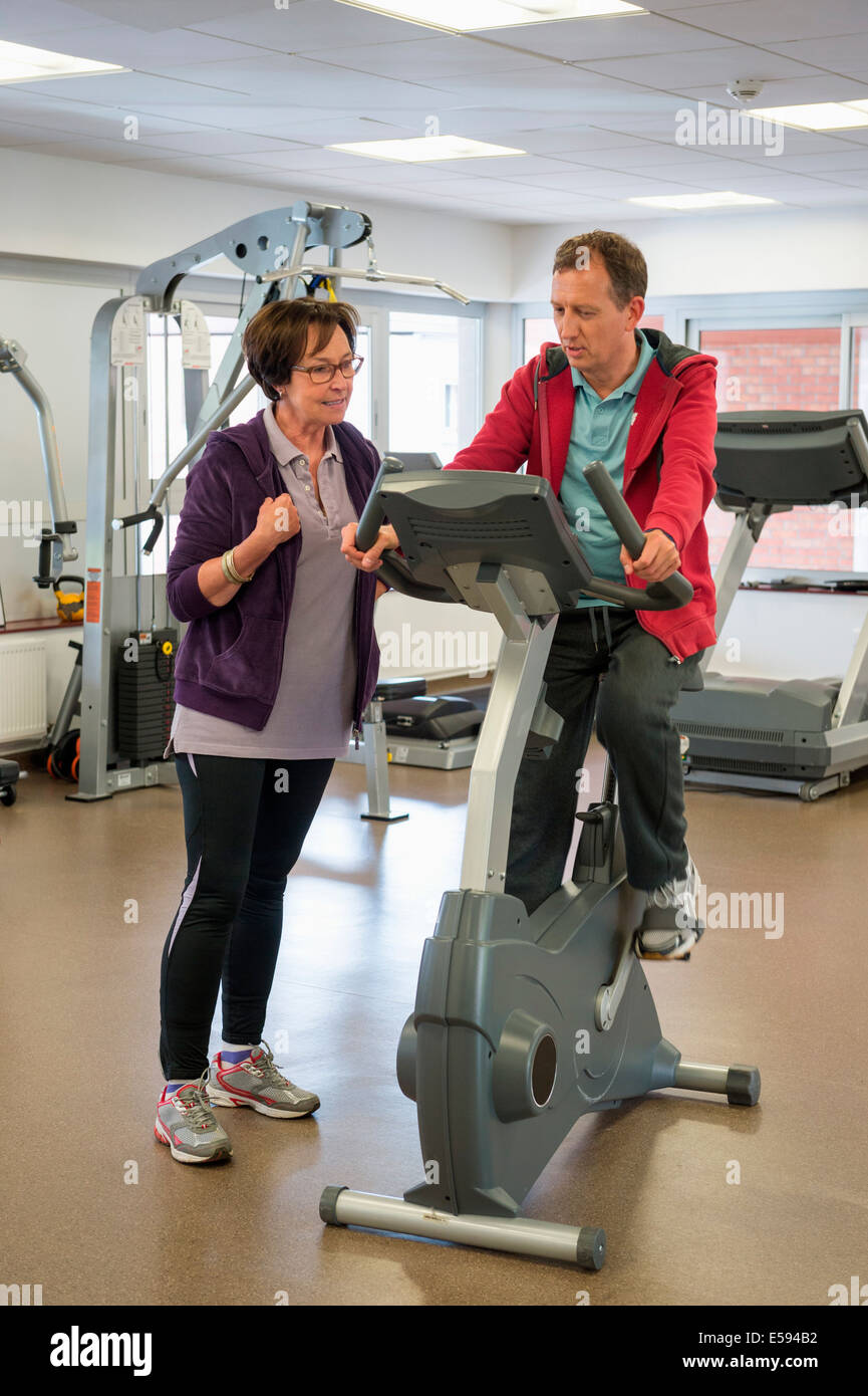 Trainer helping a woman with the cycle in a gym Stock Photo - Alamy
