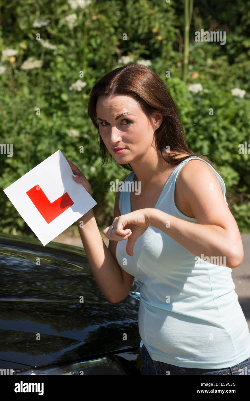 Woman driver holding L plate and thumbs down for a failure driving test ...