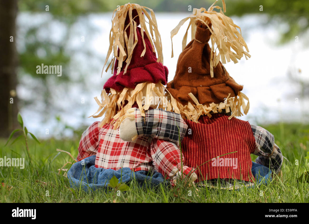 Boy and girl scarecrows back view sitting in grass by lake Stock Photo ...