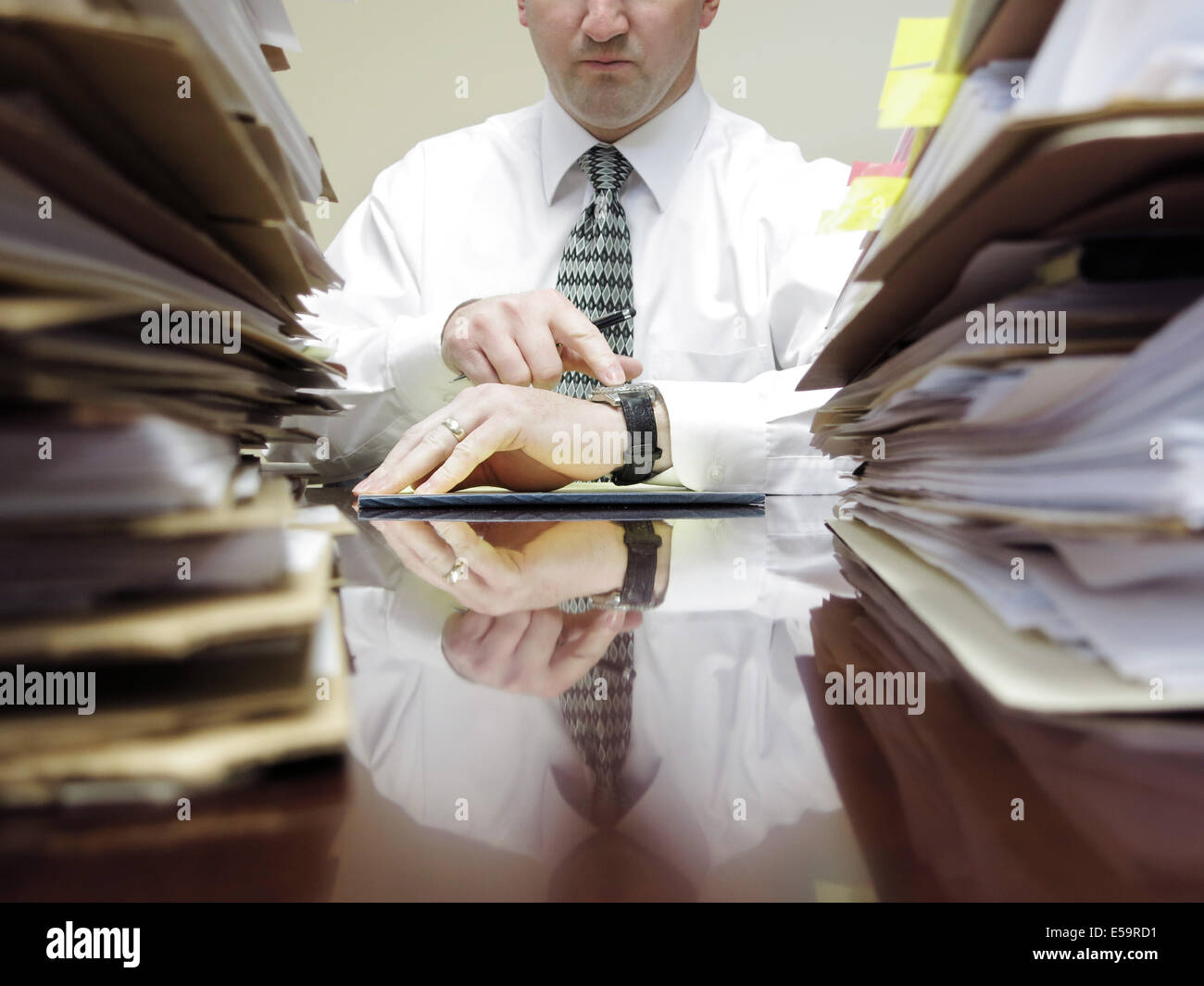 Businessman sitting at desk with pad of paper and piles files pointing ...