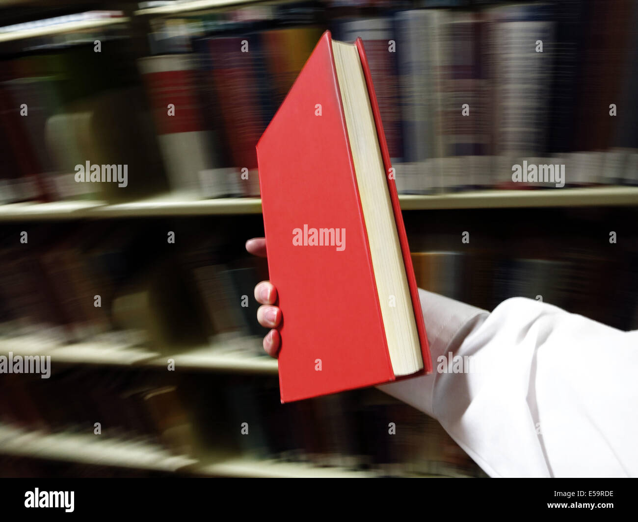 Hands holding a red book with library in background Stock Photo - Alamy