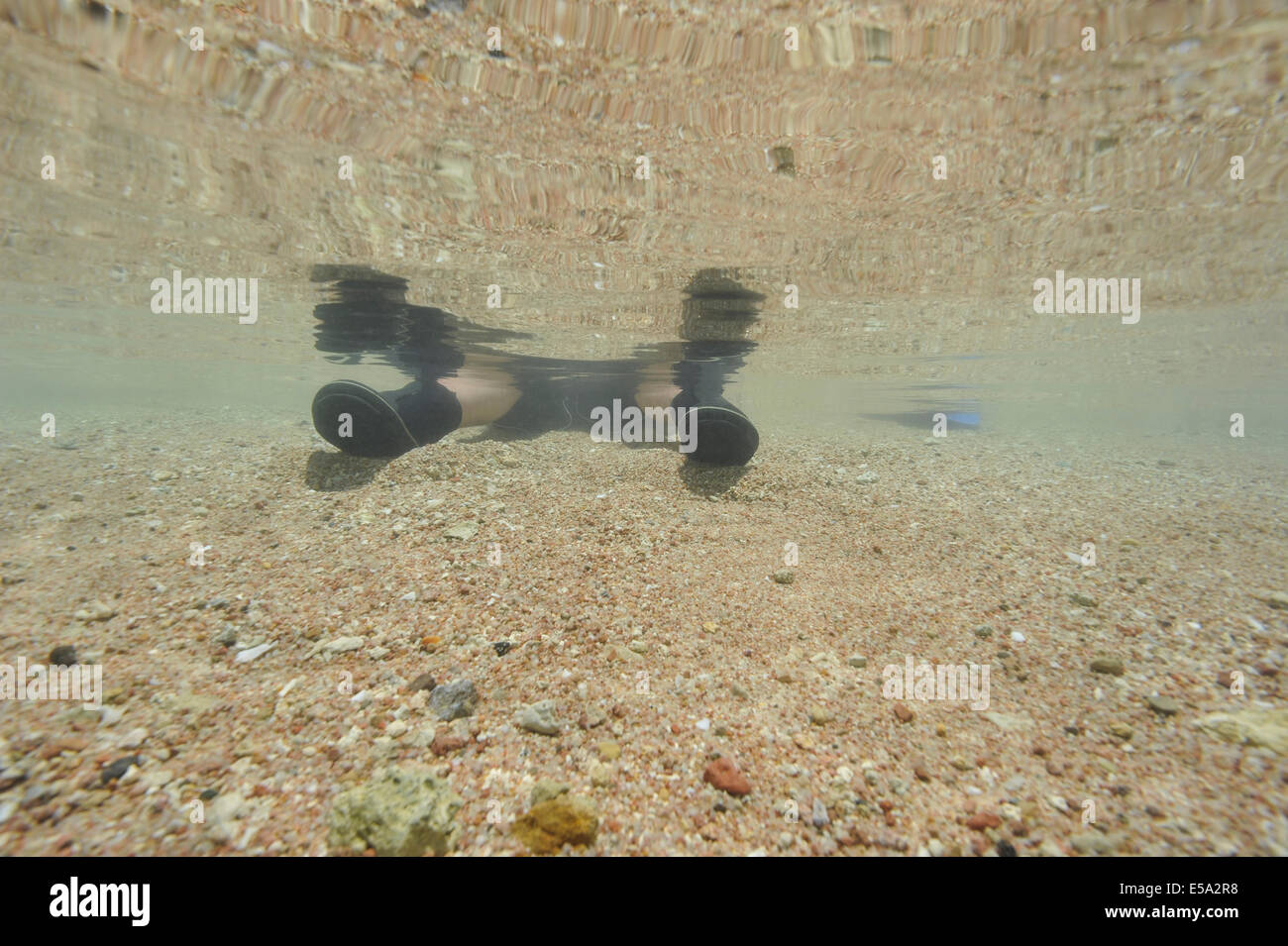 Underwater view of person sitting on beach in shallow water at tropical ...