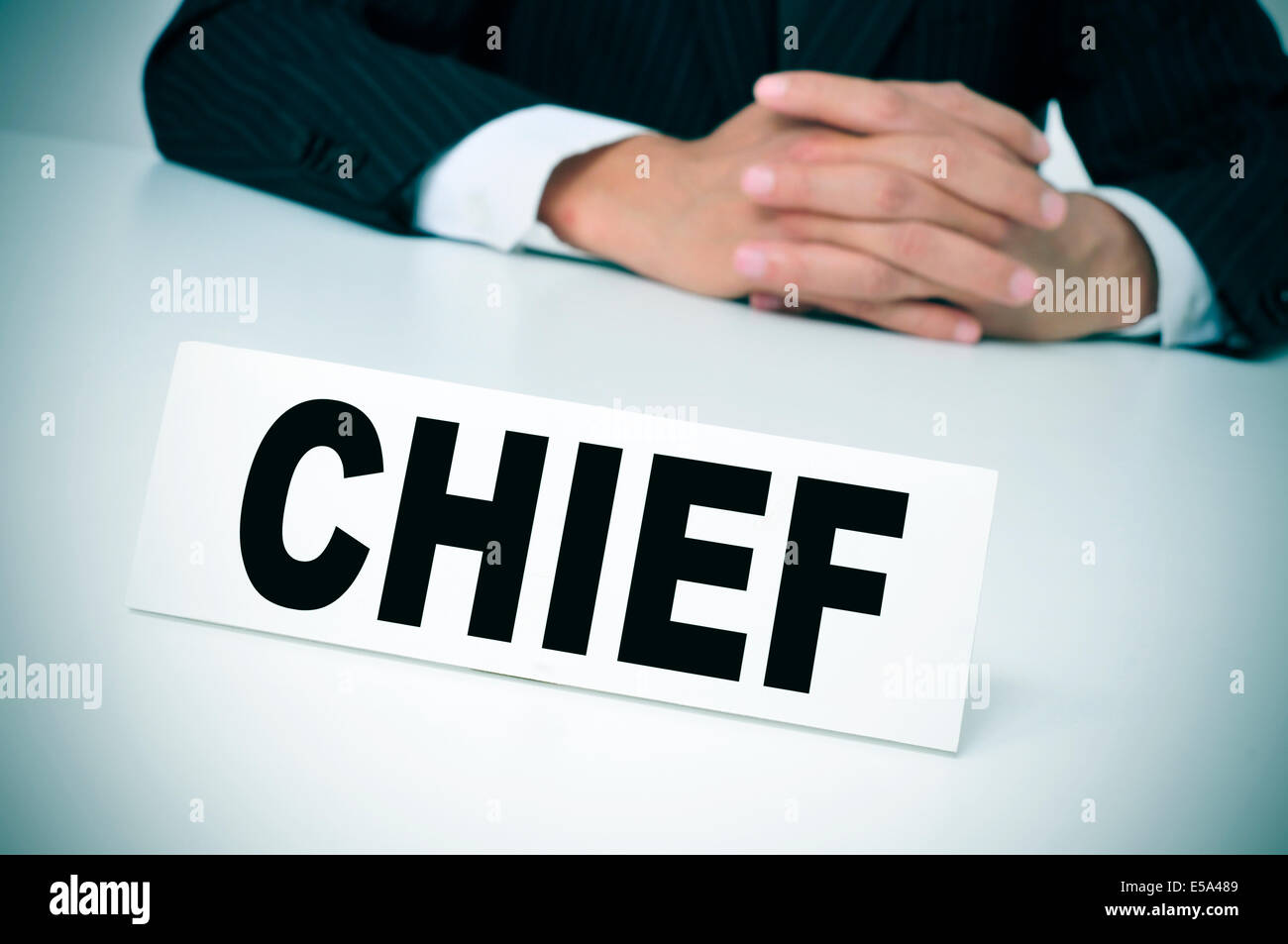 a man wearing a suit sitting in a desk with a signboard in front of him ...